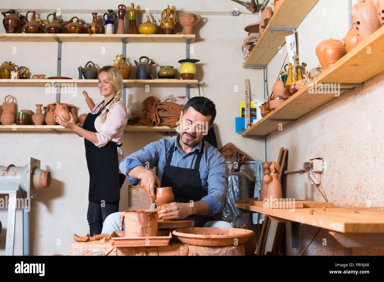 Workers in ceramics studio with pottery wheel and various clay vessels ...