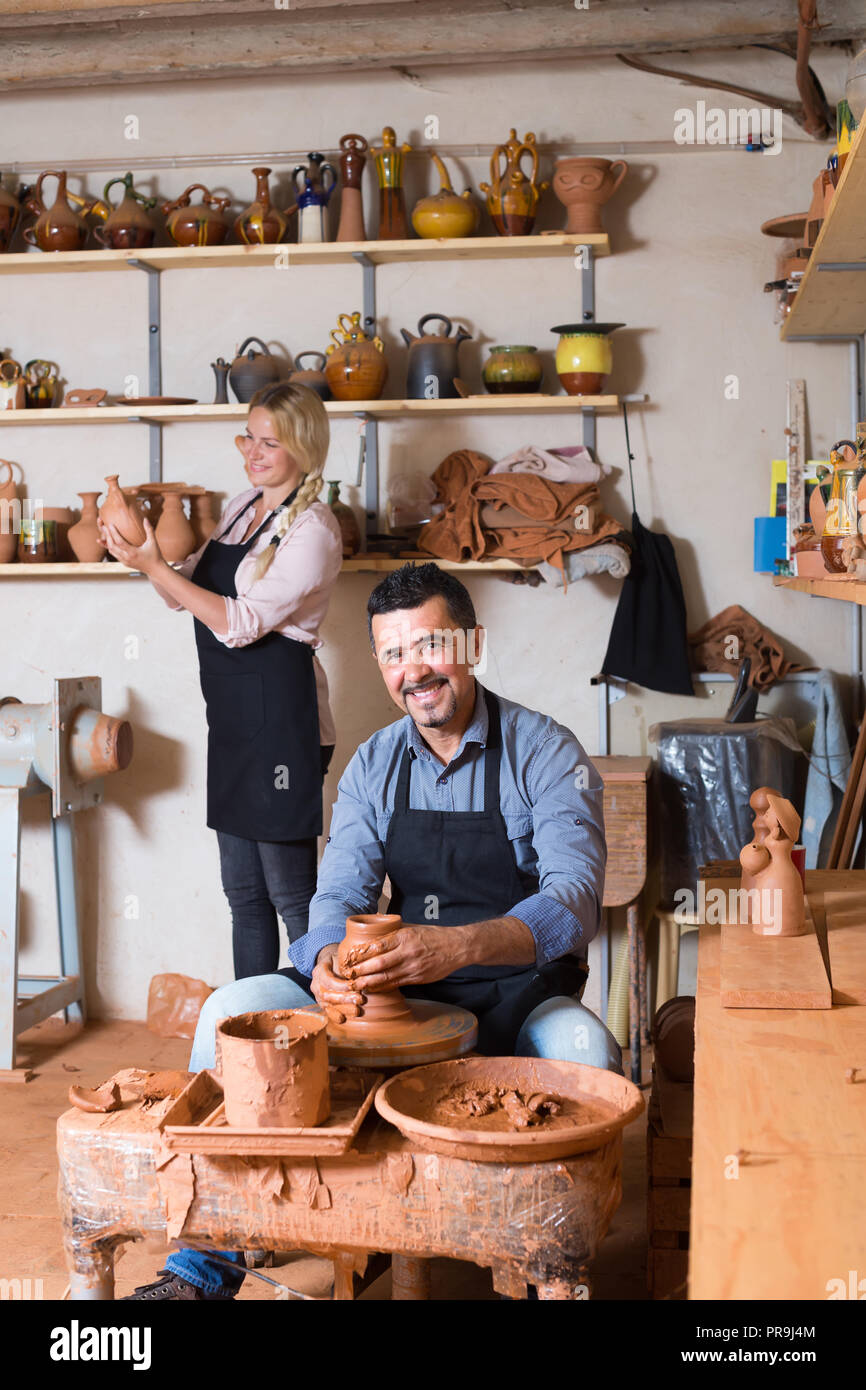 two friendly smiling potters making ceramic vessels on pottery wheel in ...