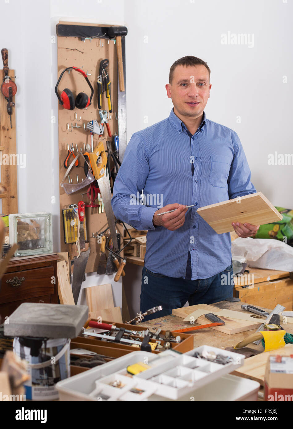 Smiling adult woodworker working with wood plank at workplace Stock ...