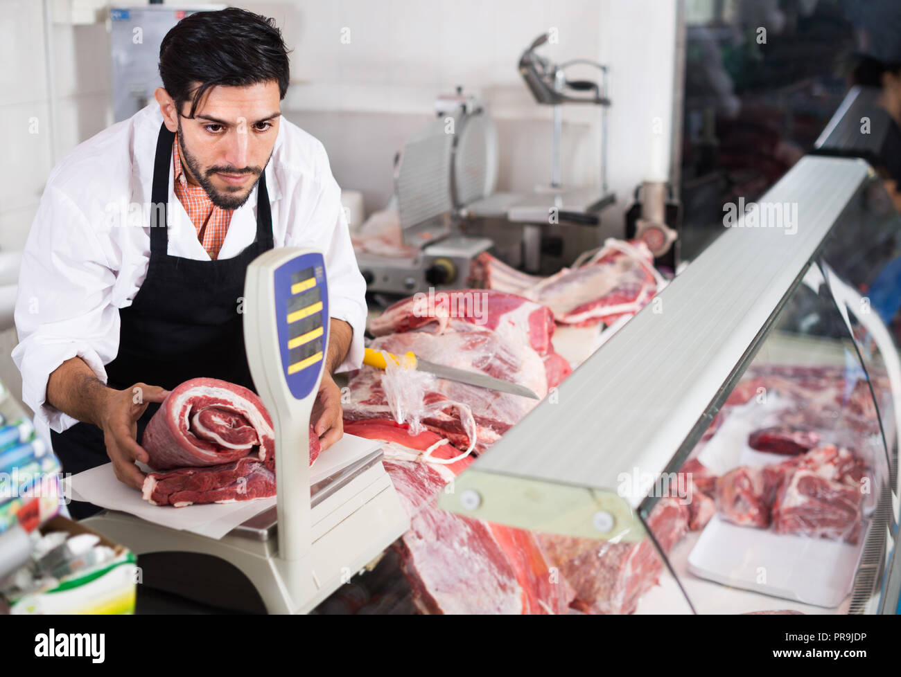 Adult man butcher is weighing meat for client in food shop Stock Photo ...