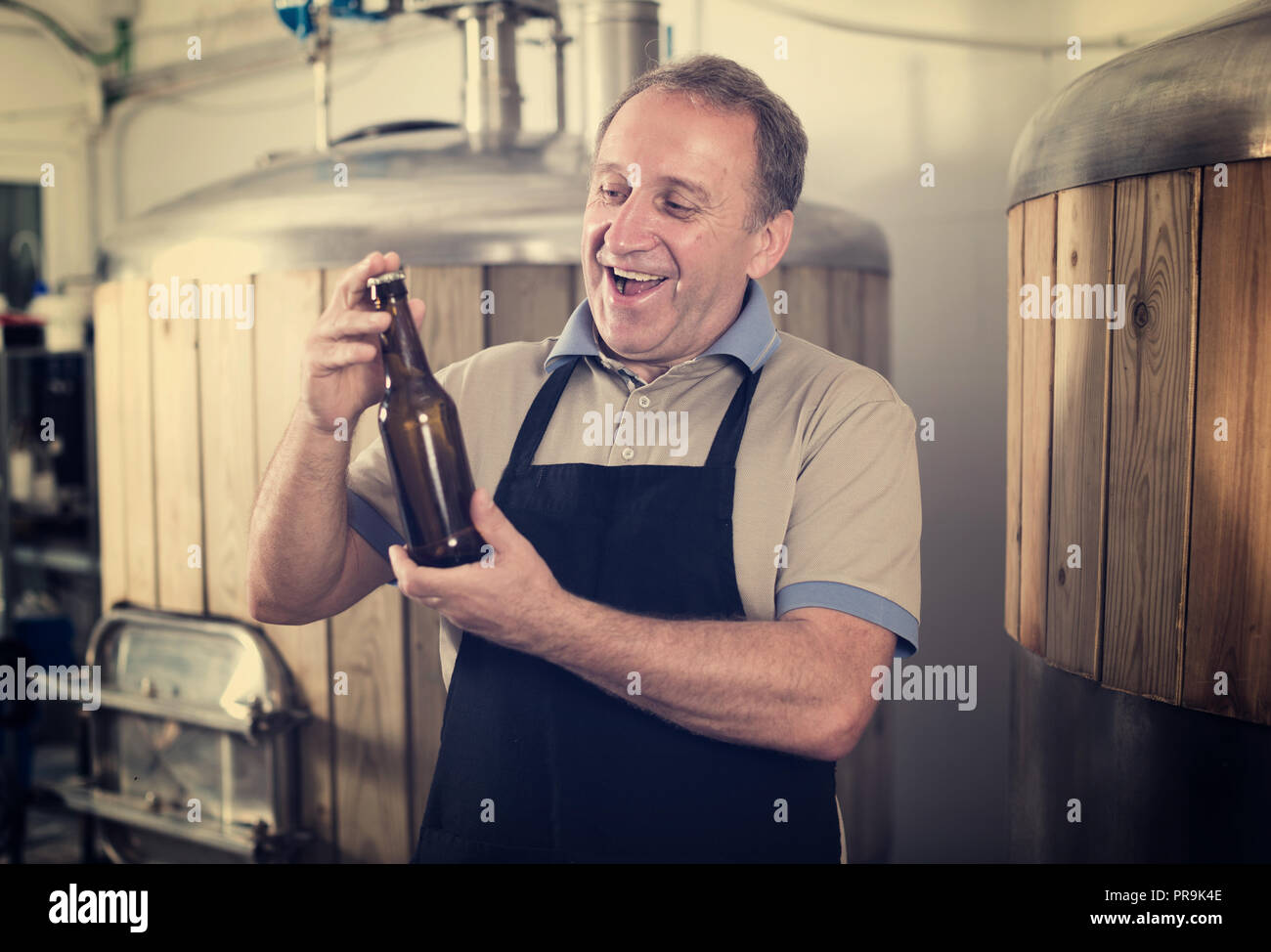 Brewer is standing with bottle for beer on his workplace indoor Stock ...