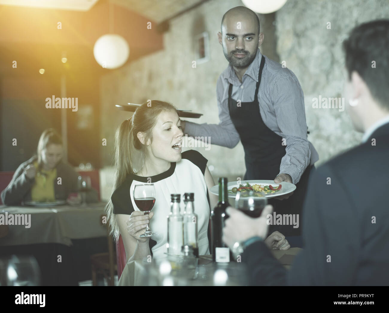 Smiling guy waiter serving meals to positive couple at cafe Stock Photo ...