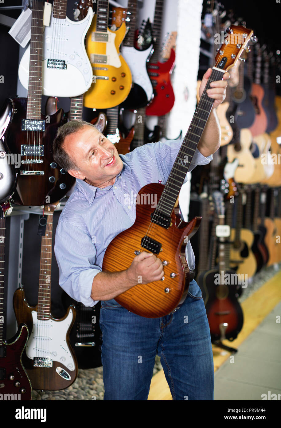 Adult cheerful positive smiling guitarist is playing on electric guitar ...