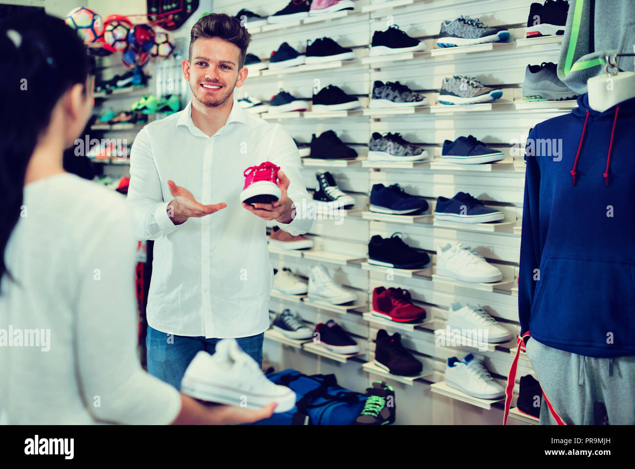 Young smiling man seller assisting girl in choosing sneakers in sports ...
