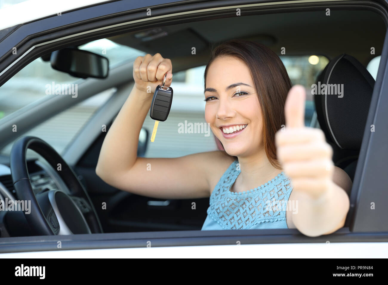 Happy car owner looking at camera holding a key gesturing thumbs up ...