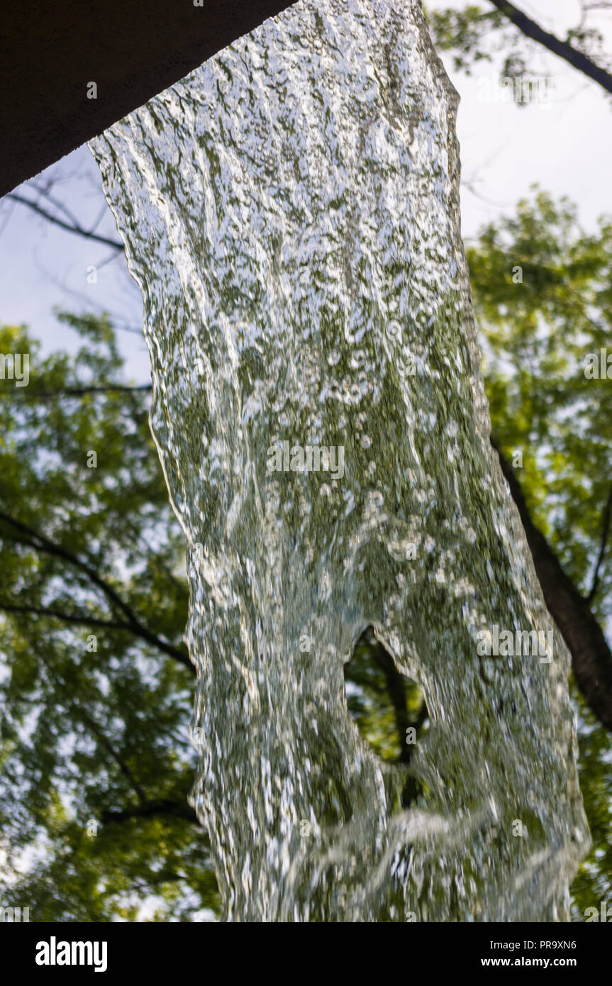 transparent falling water vertical flows against a blue sky and green ...
