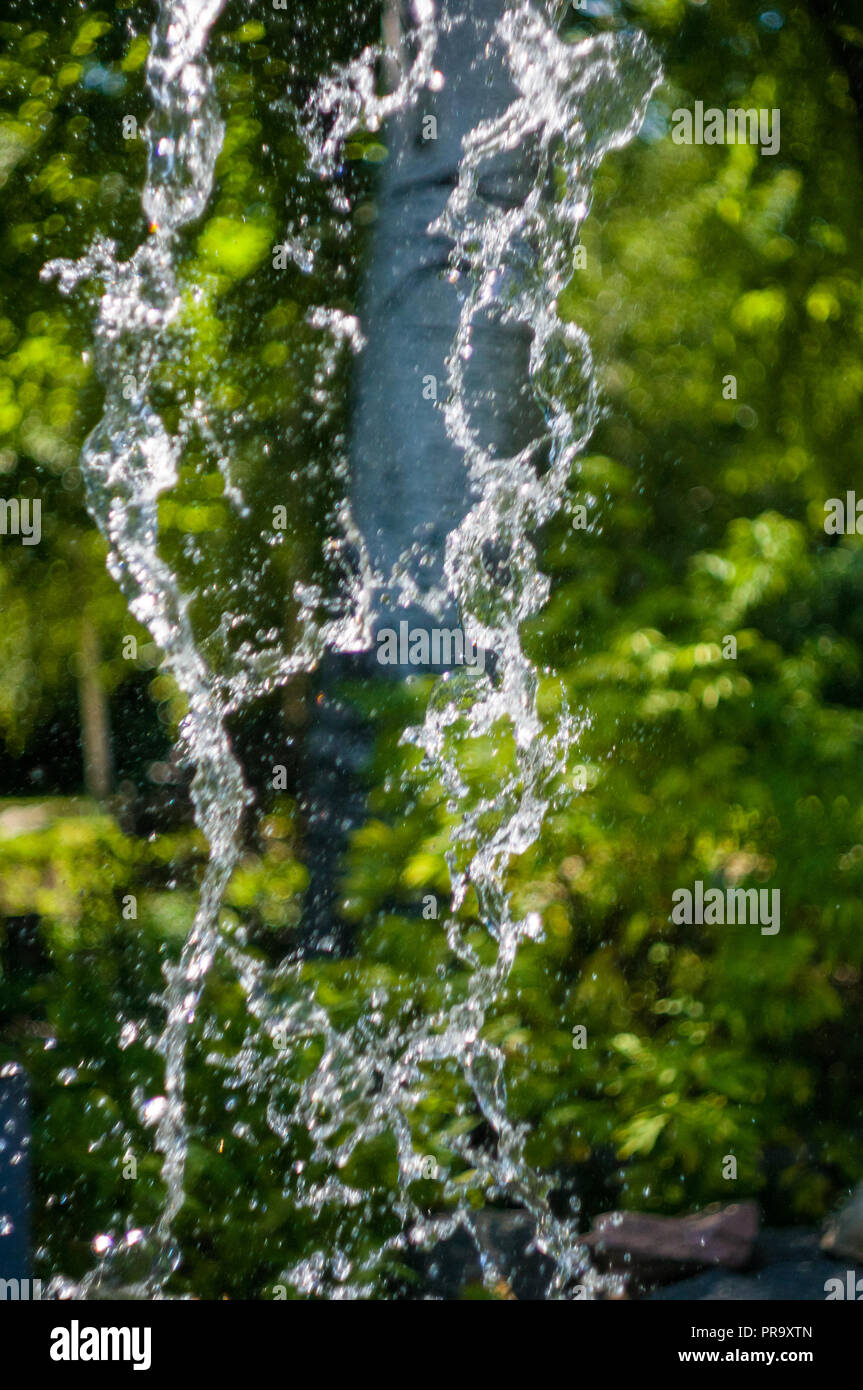 transparent falling water vertical flows against a blue sky and green ...