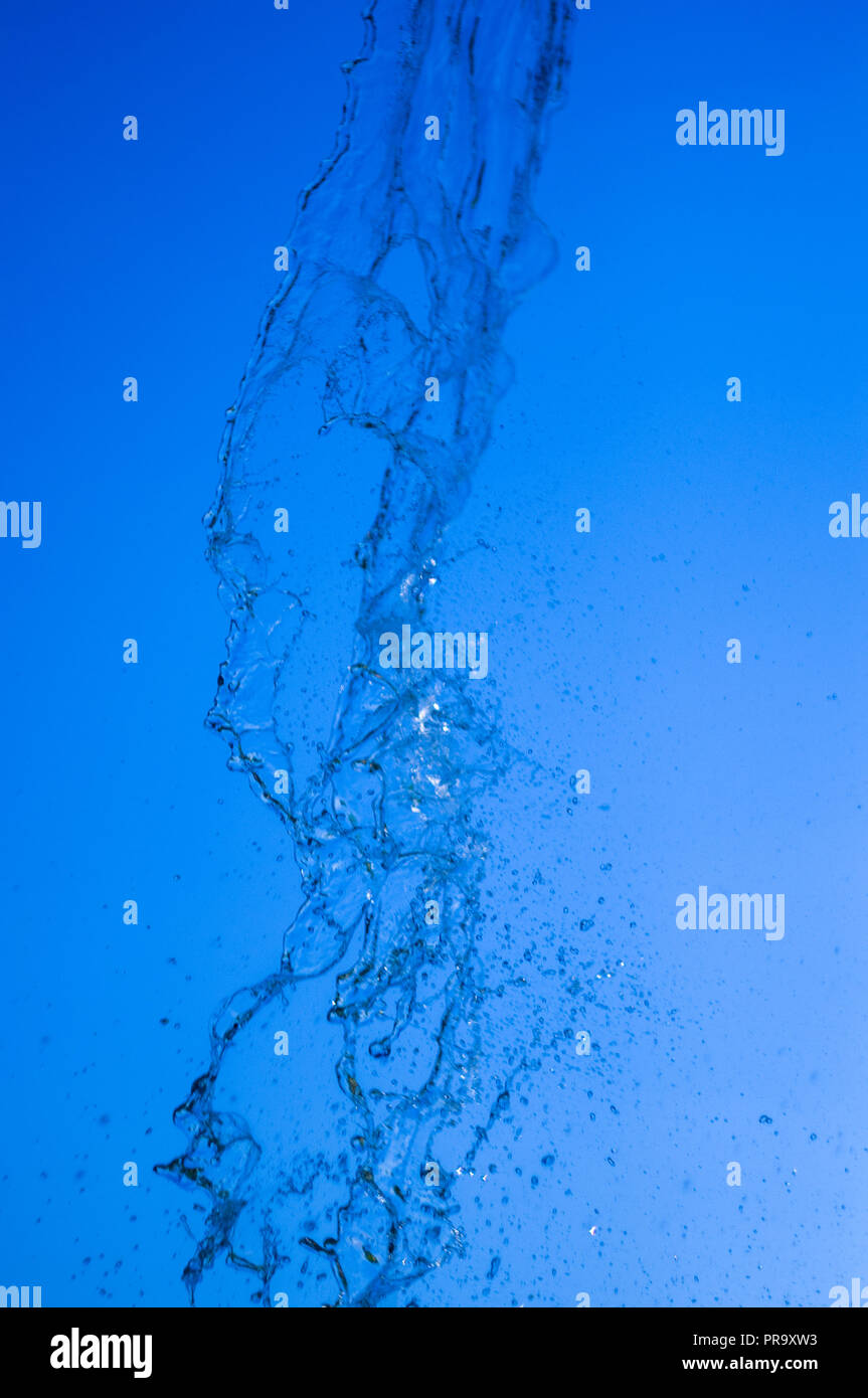 transparent falling water vertical flows against a blue sky and green ...