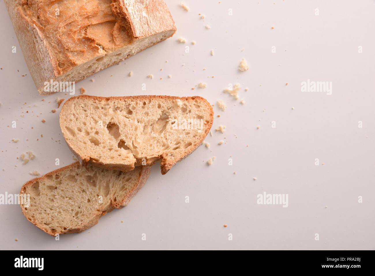 Loaf of bread cut into two slices on white table close up. Top view ...