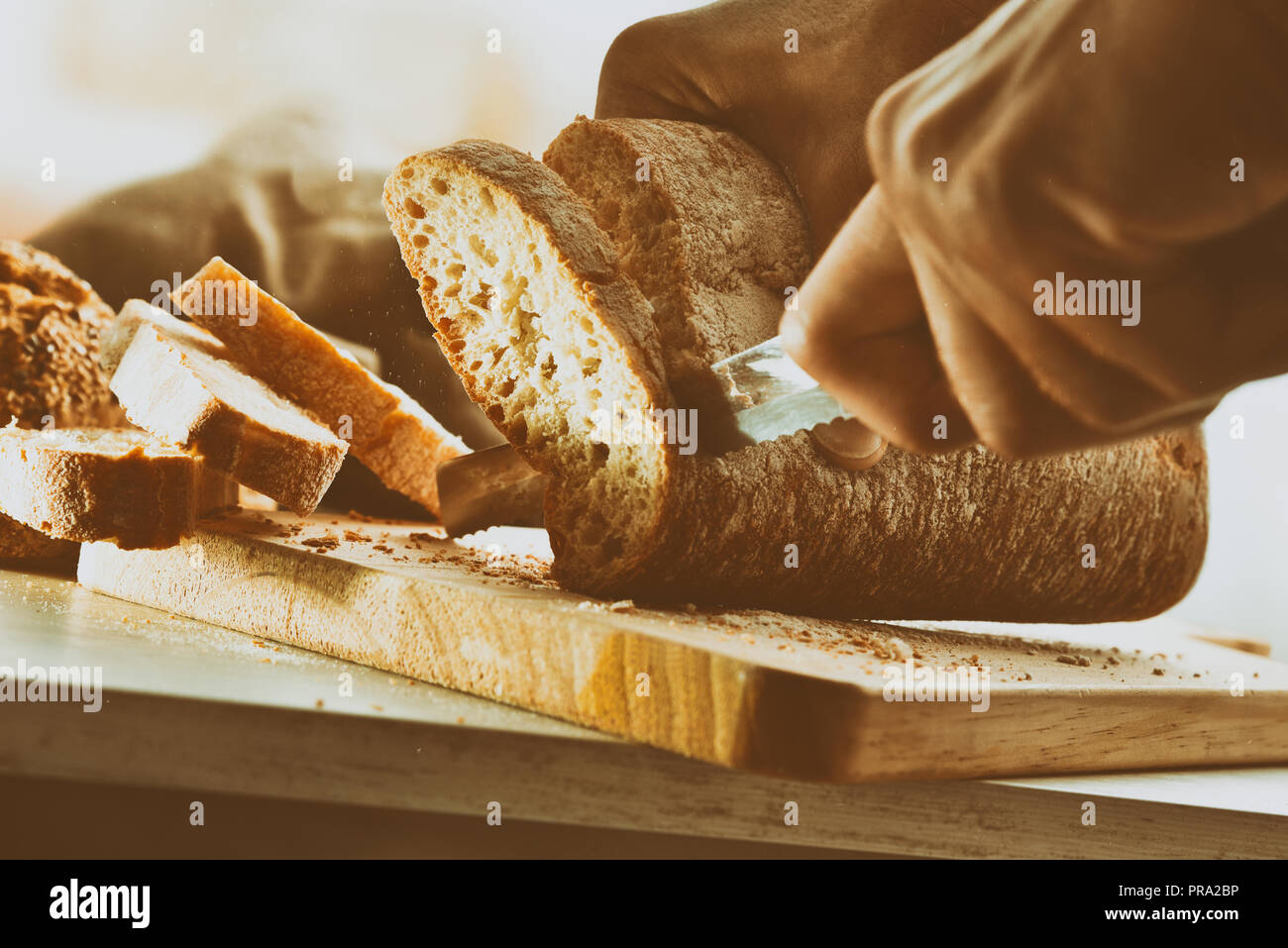 Chef slicing bread in slices on a cutting board in a kitchen bench ...