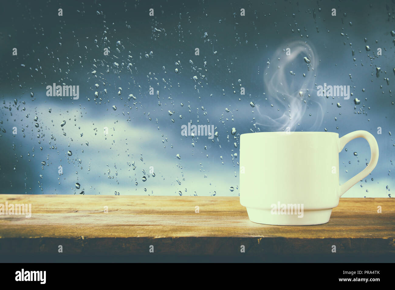 coffee cup on a rainy day over wooden table and window with rain drops ...