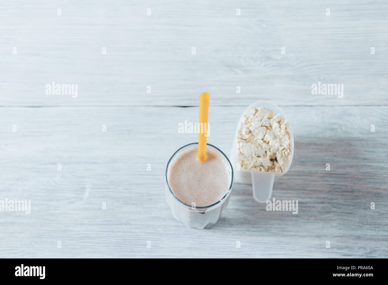 Whey protein shake in glass with straw next to measuring spoon of dry ...
