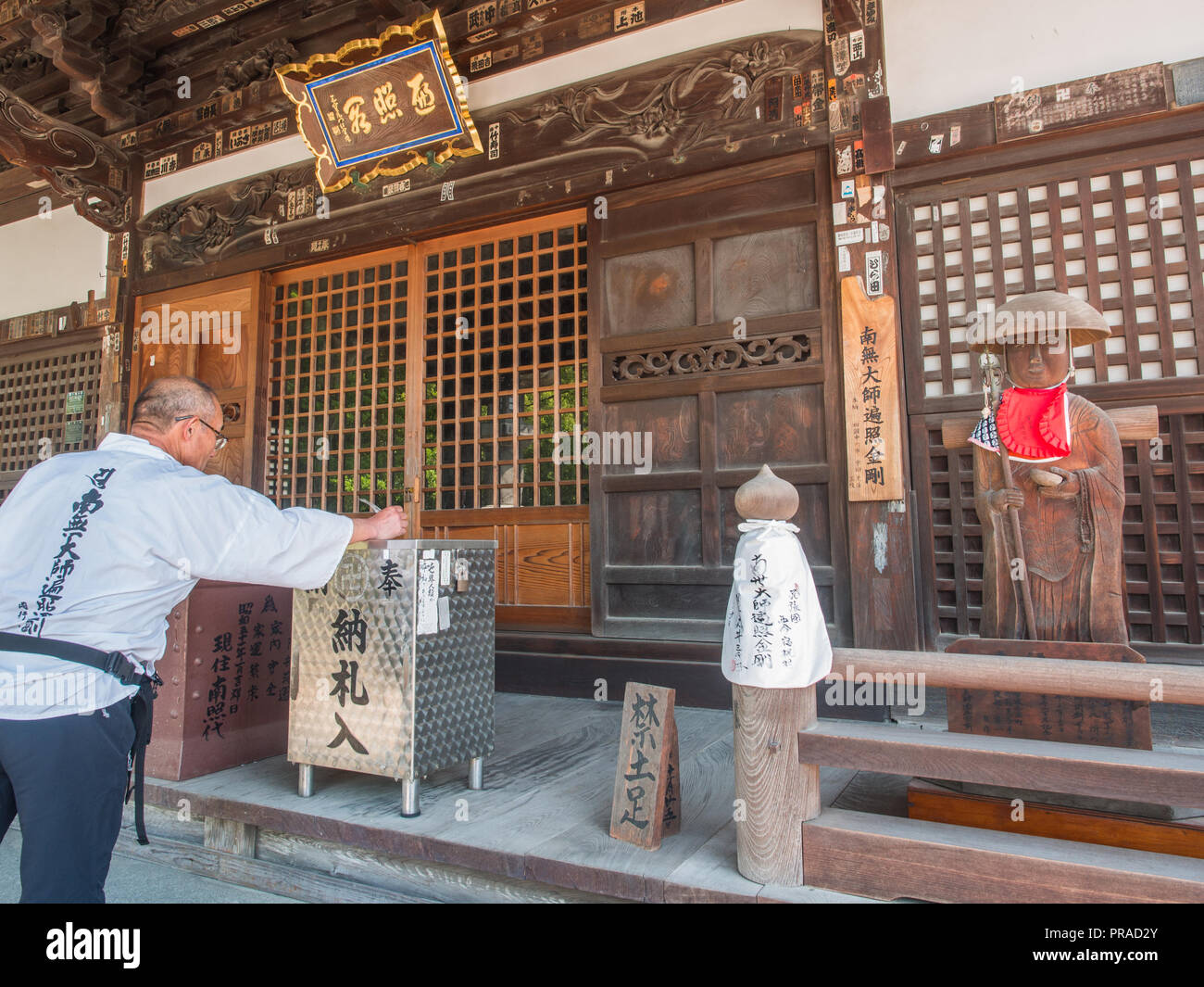 Henro pilgrim putting osame fuda name slip, into collection box ...