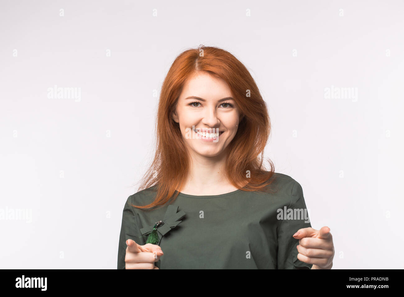 Cheerful young red-haired woman pointing at the viewer with her finger ...