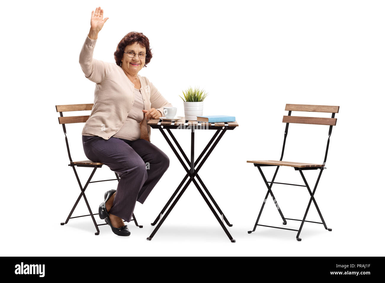 Senior lady sitting at a coffee table and waving isolated on white ...