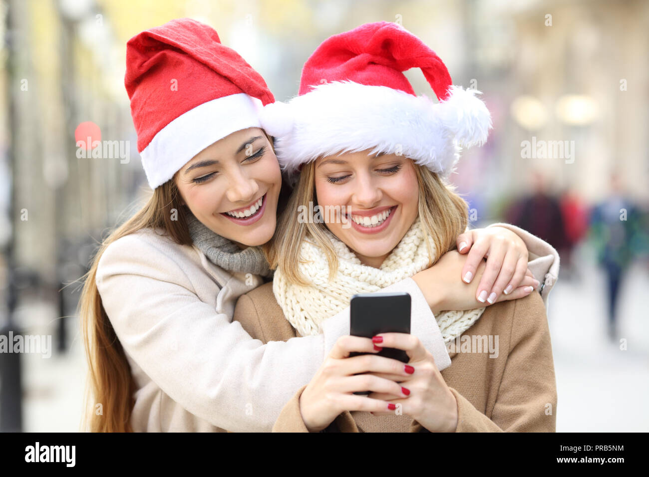 Two happy friends wearing santa hats texting on a phone on christmas on ...