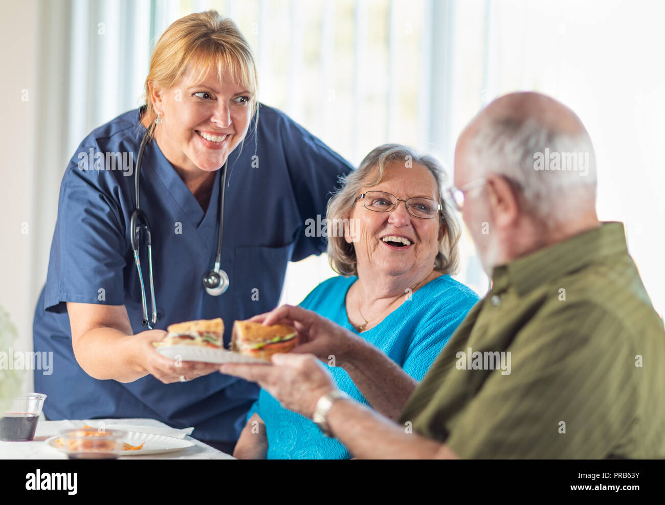 Female Doctor or Nurse Serving Senior Adult Couple Sandwiches at Table ...