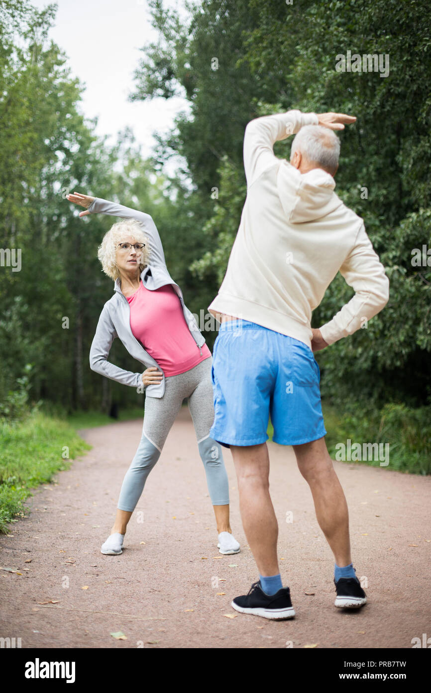 Active mature couple in sportswear doing physical exercise in park ...