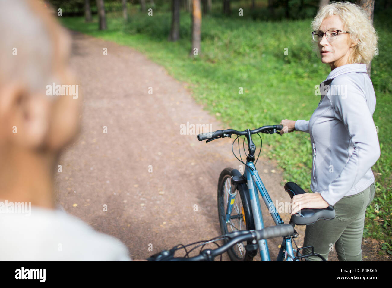 Blonde active woman with bicycle talking to her husband while walking down country road Stock ...