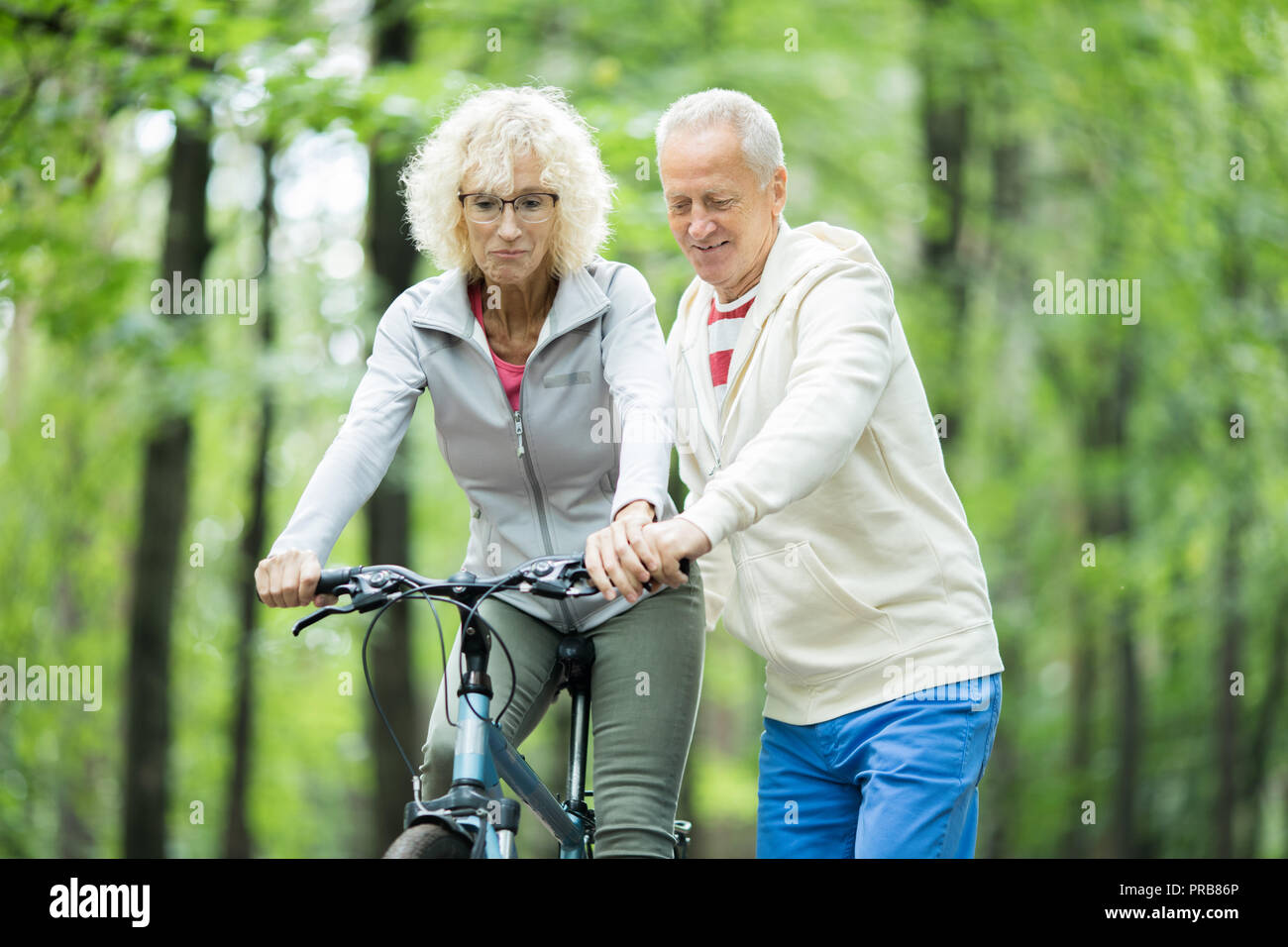 Aged man teaching his wife how to ride bicycle while chilling in ...