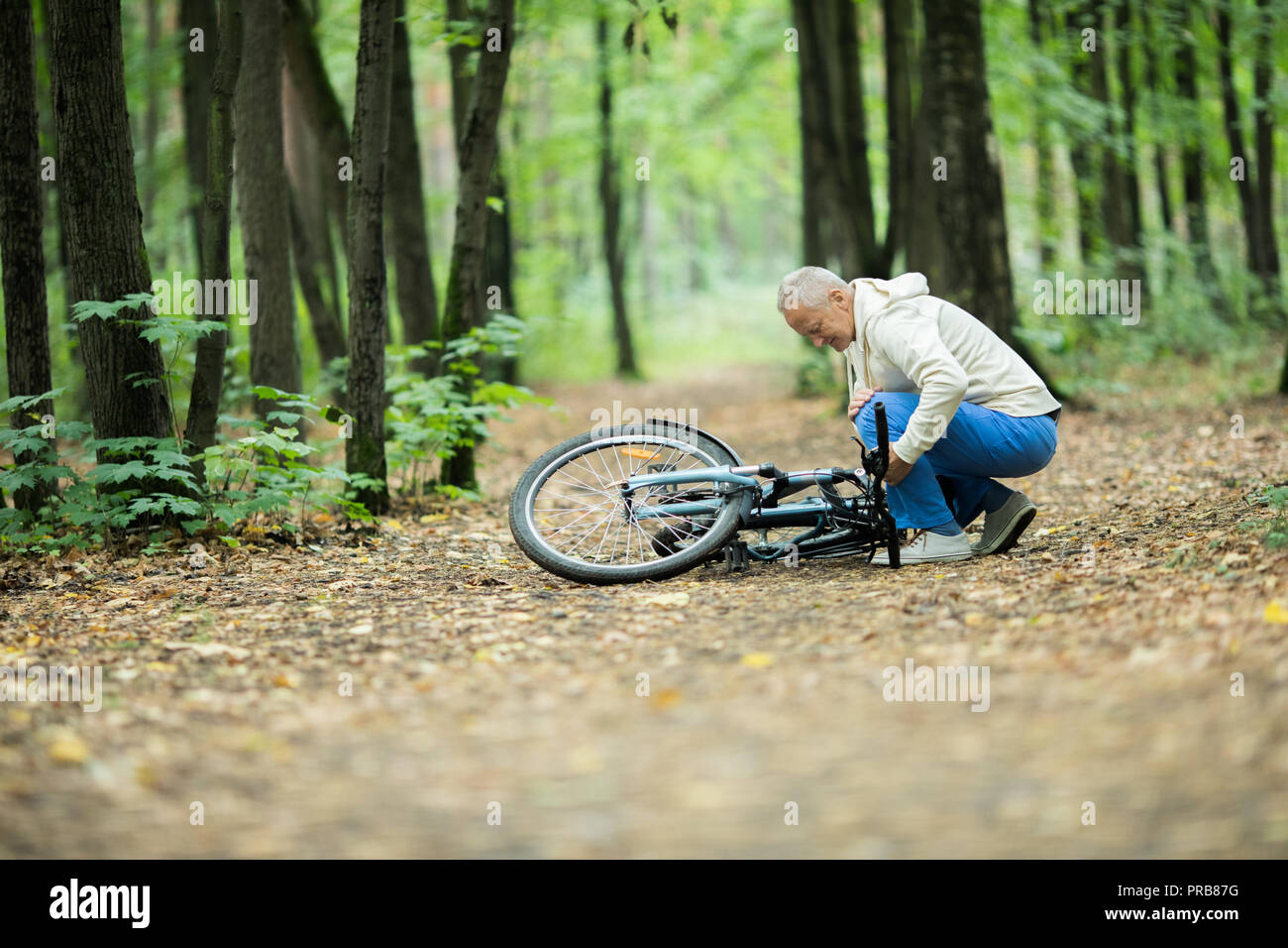 Senior sportsman squatting above his bicycle on the ground or lying it ...