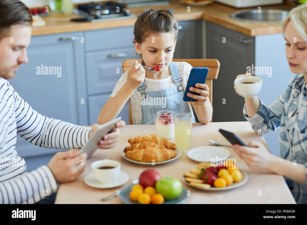 Modern family using mobile gadgets while having breakfast by served ...