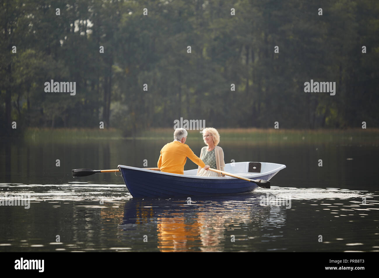Smiling beautiful curly-haired senior lady in cardigan sitting on boat ...