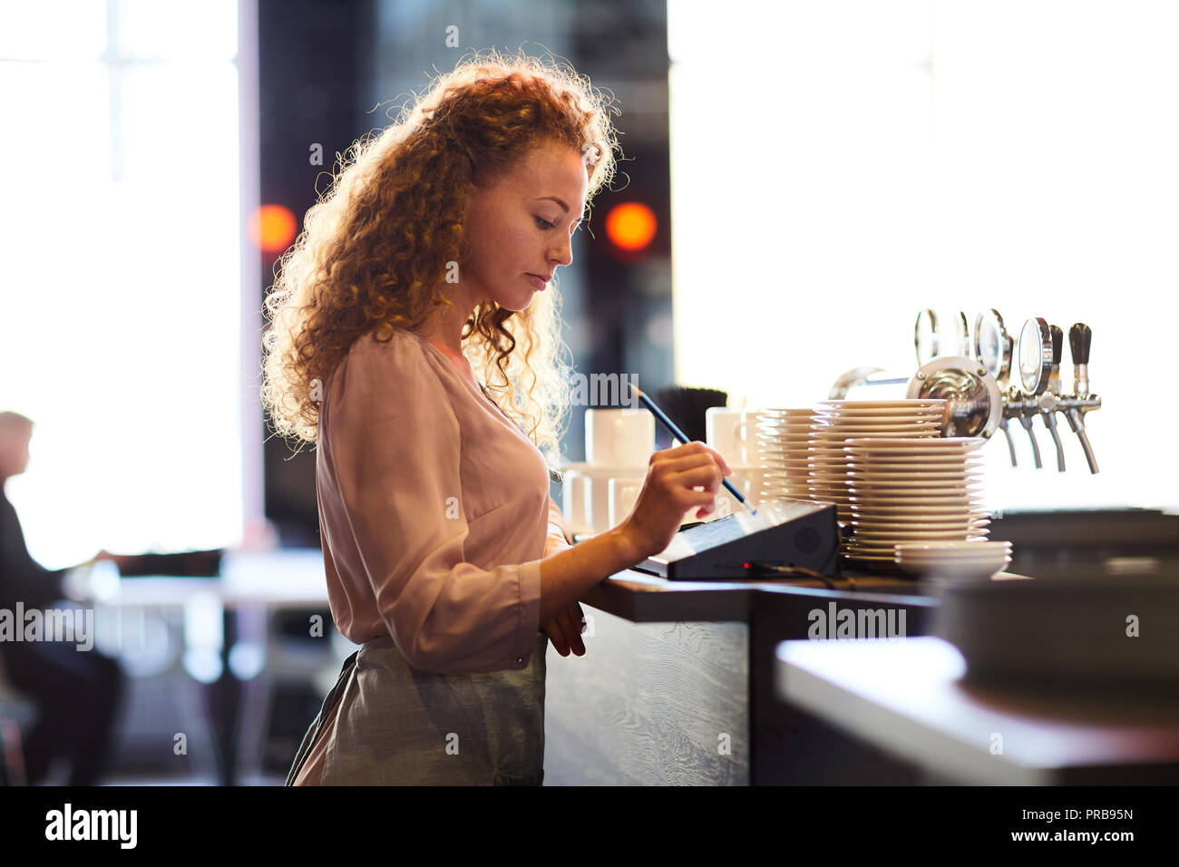 Serious pensive attractive curly-haired waitress standing at bar ...
