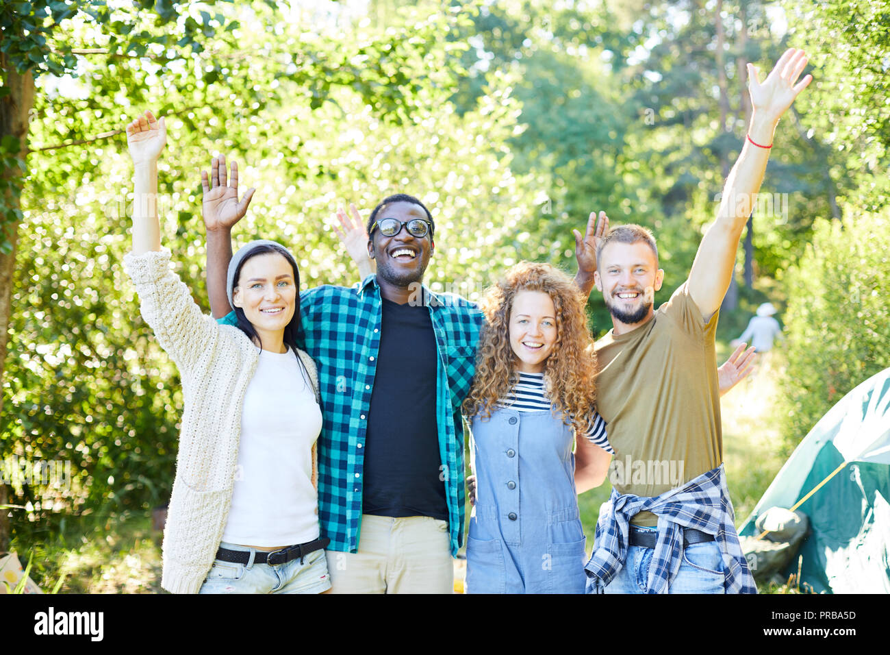 Four young joyful friends raising their hands while having fun on ...