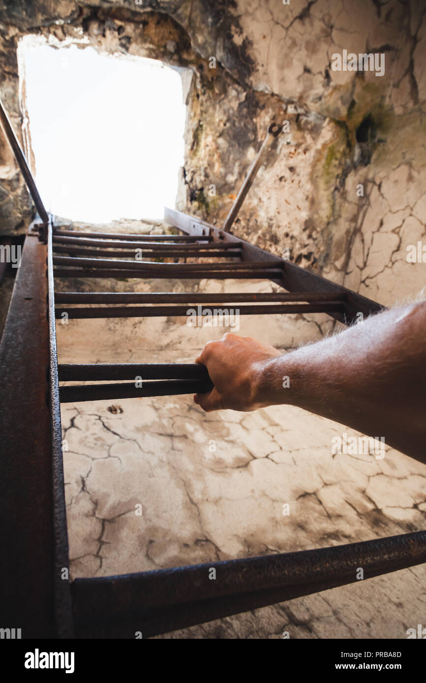 Rusty metal ladder with male hand holding it, empty mine interior with ...