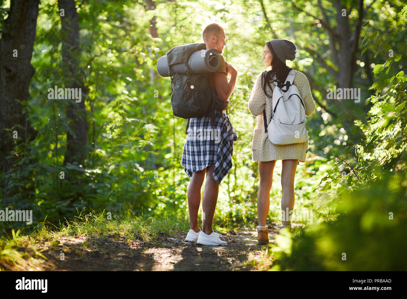 Back view of couple of campers with backpacks walking down forest path ...
