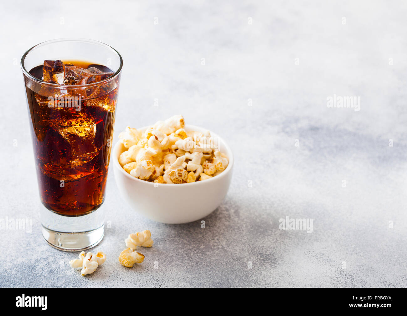 Glass of cola soda drink with ice cubes and whitel bowl of popcorn ...