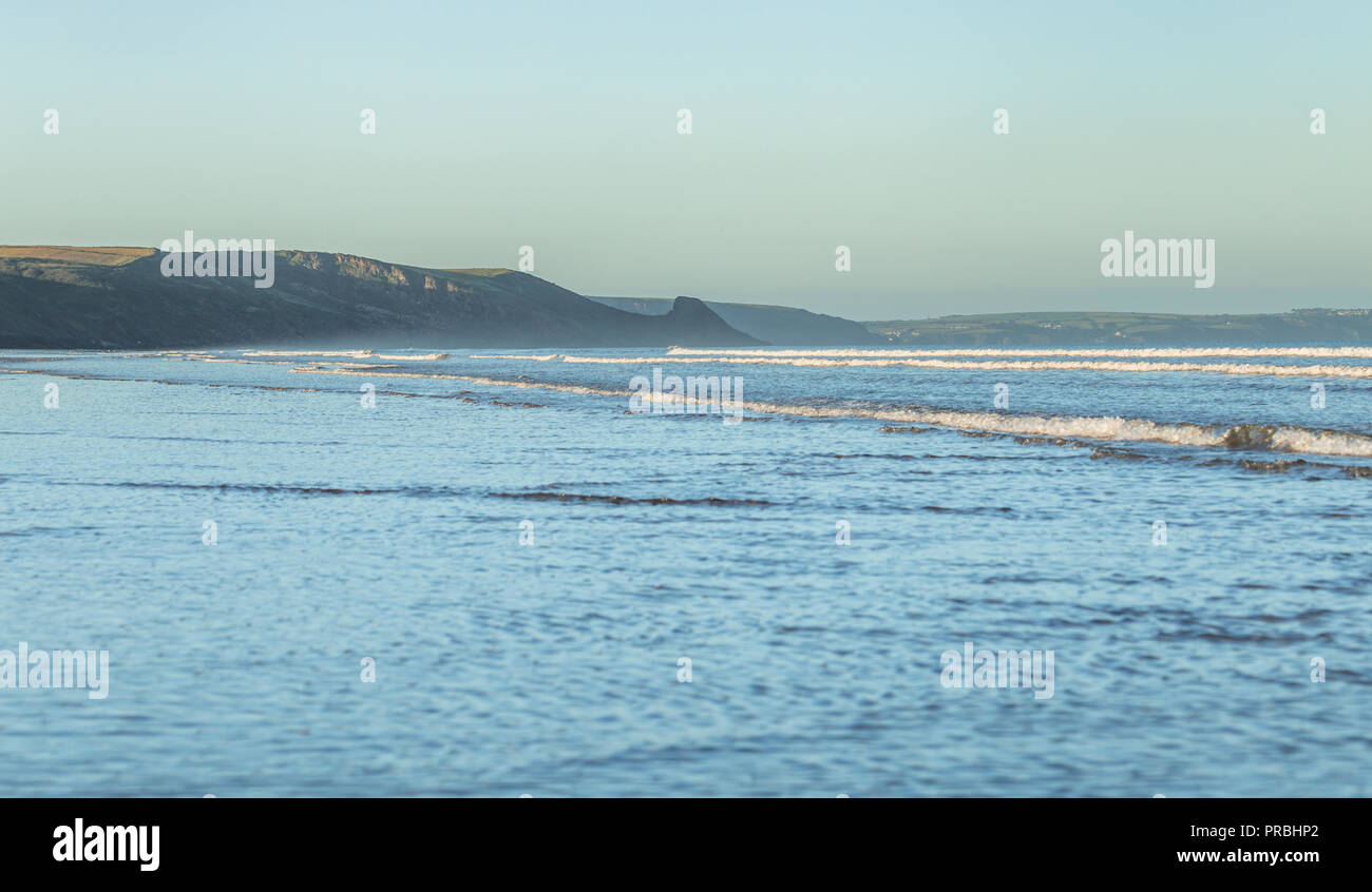 Long blue tidal waves with scenic green cliffs in background of Newgale ...
