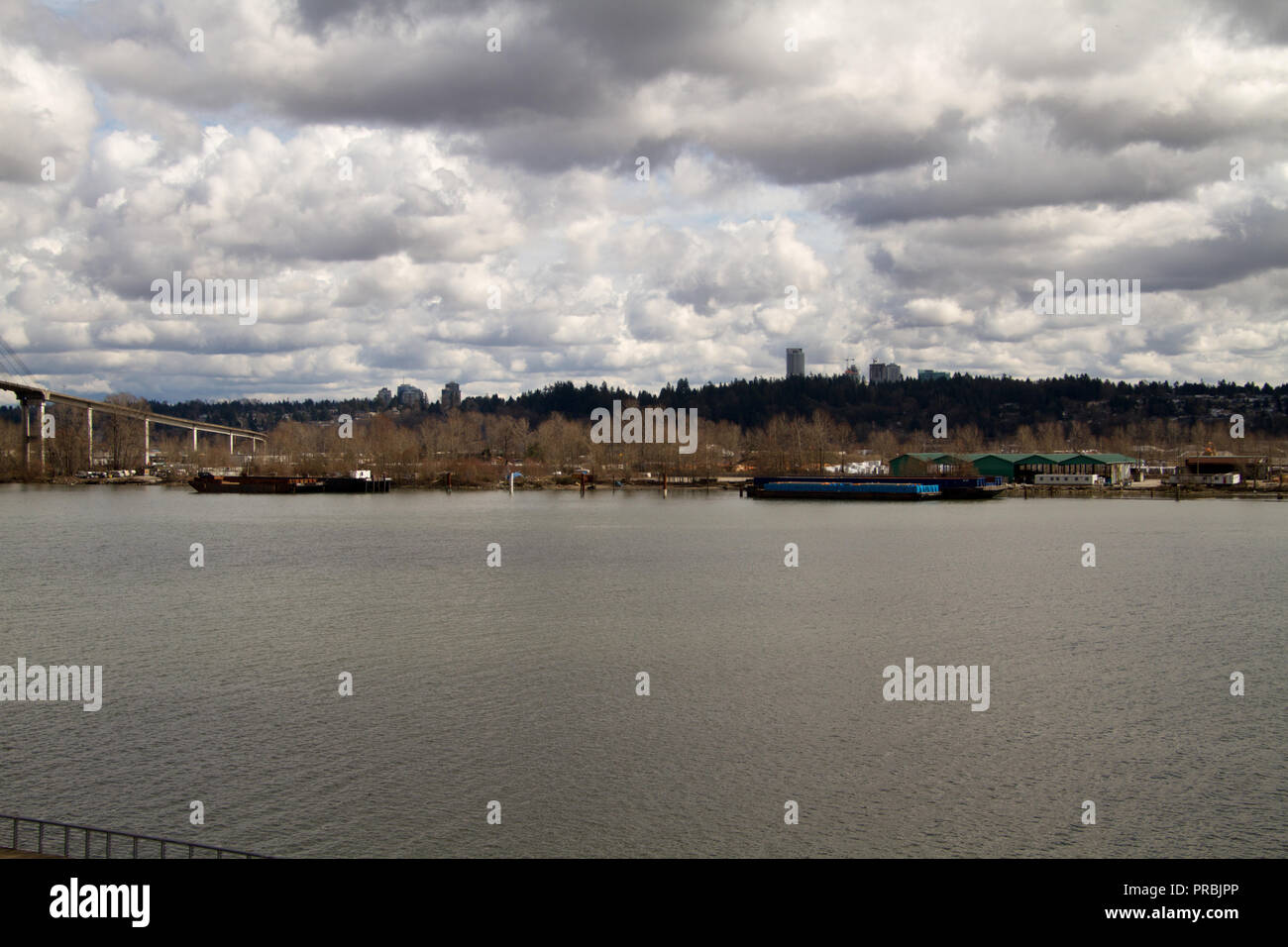 A view of a river with barges docked on the far side with a city seen ...