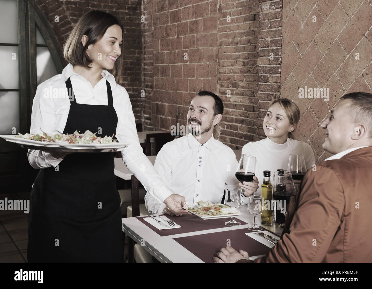 Smiling female waitress placing order in front of guests in country ...