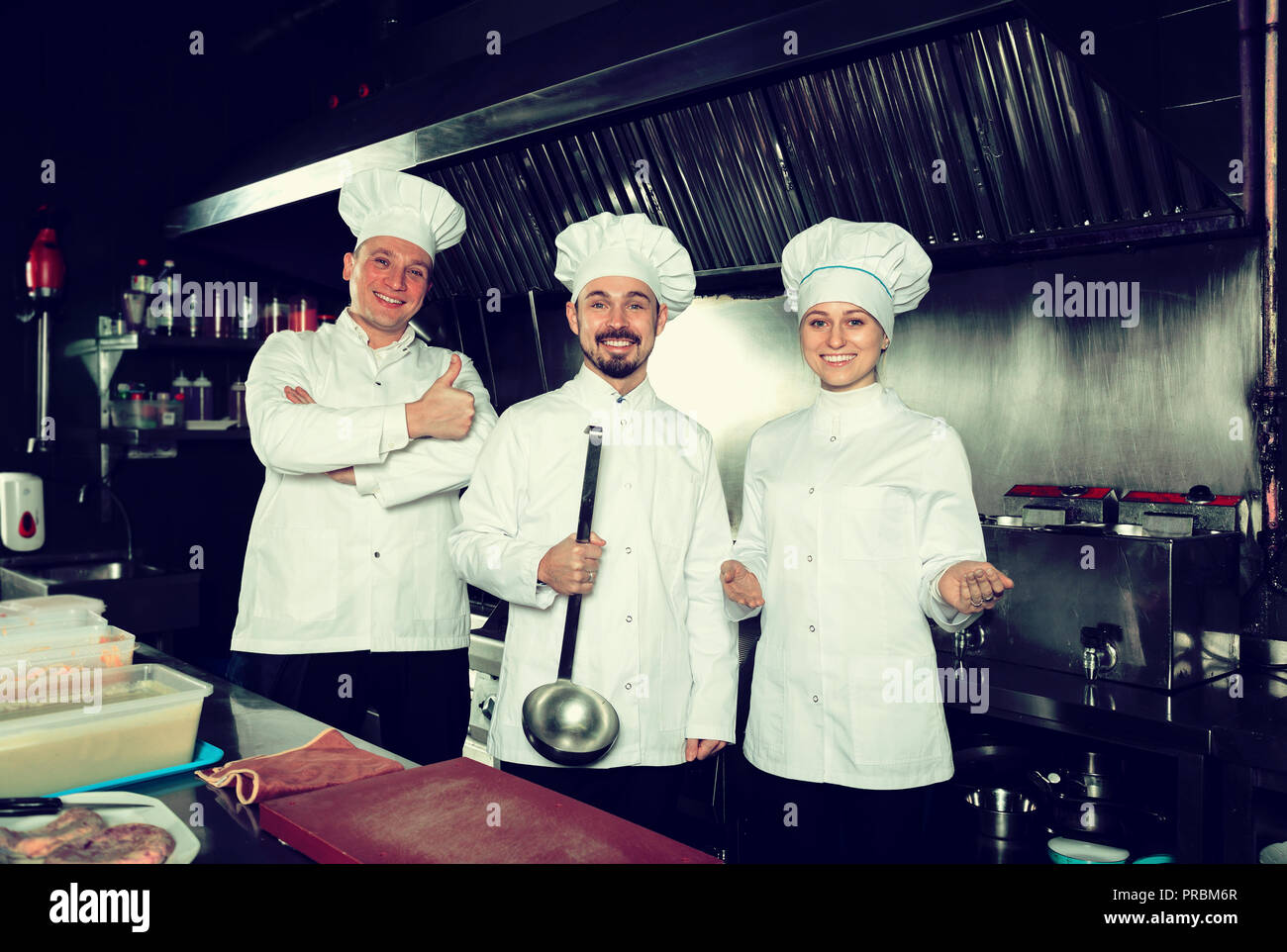Happy professional cooks welcoming to their workplace in restaurant’s ...