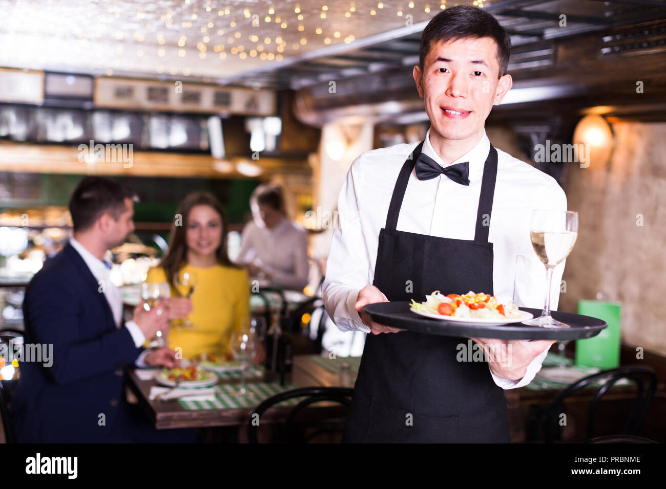 Man waiter is holding tray with wine and salad for clients in ...