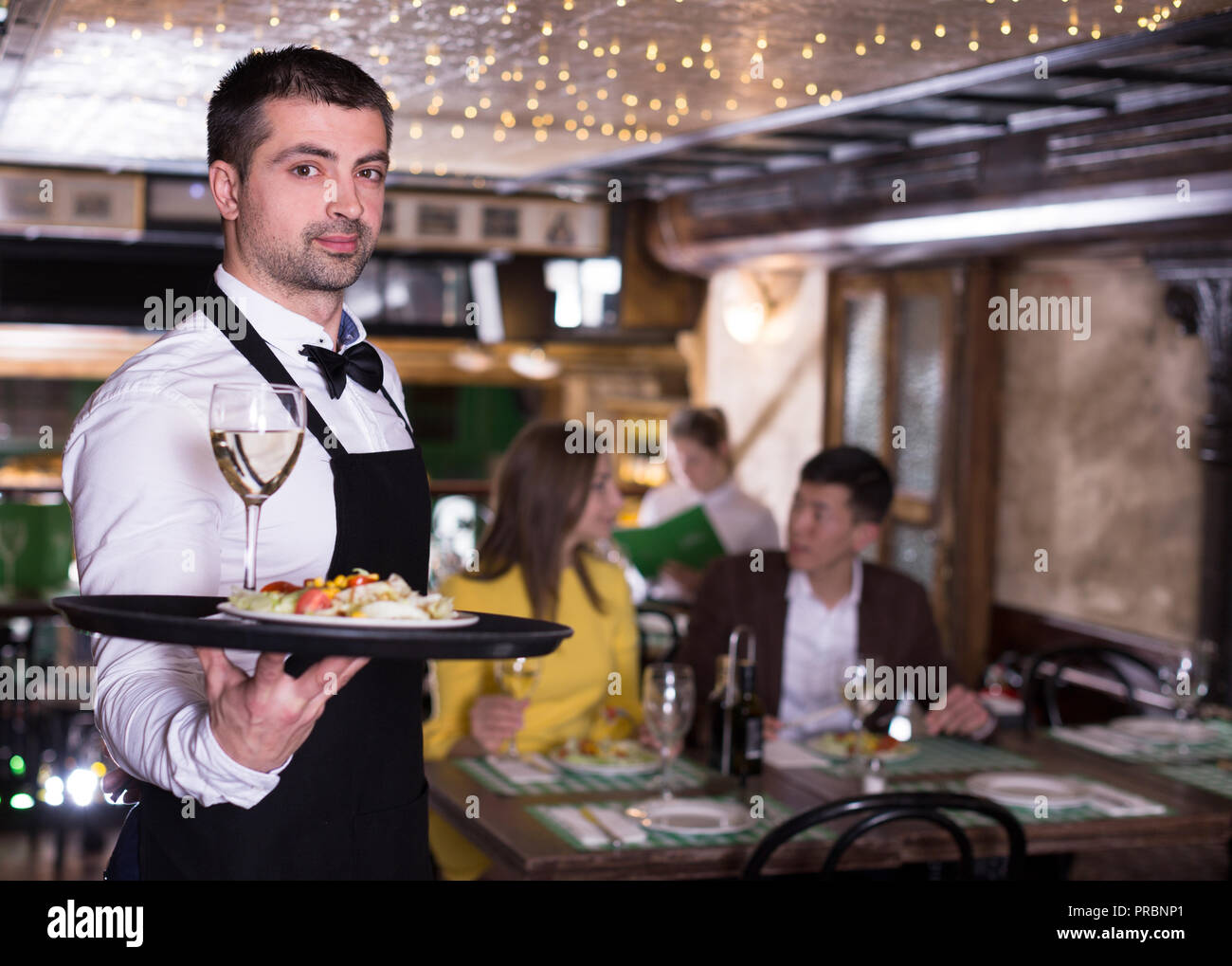 Portrait of male waiter who is holding tray with order in hall of ...