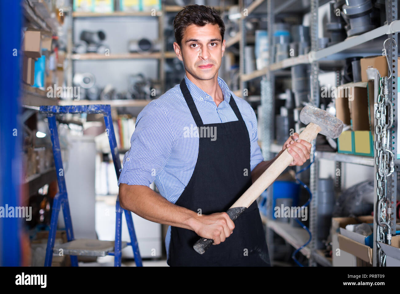 Portrait of craftsman in uniform who is standing with sledgehammer in ...