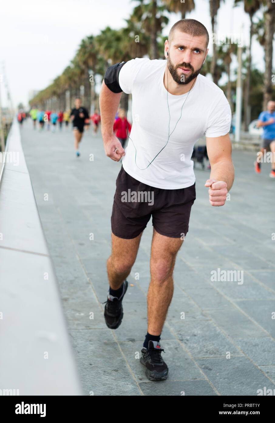 Athletic male in a white t-shirt running along the sidewalk in the city ...