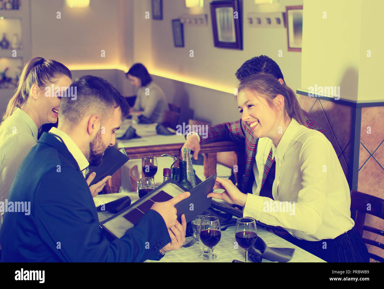 Сheerful glad positive smiling friends choosing dishes out of menu card ...