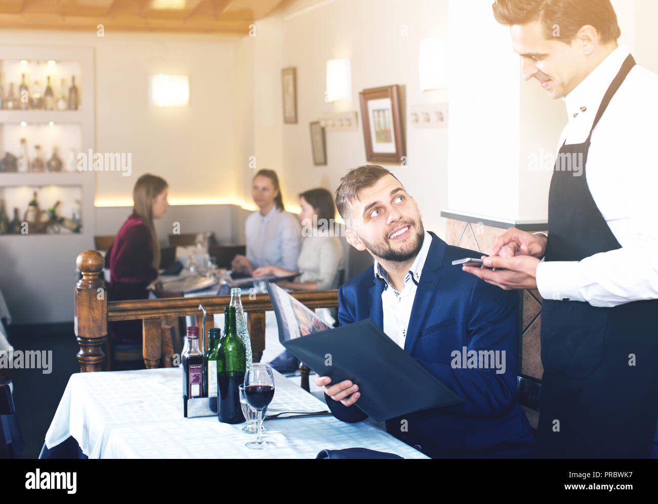 Positive waiter taking order in restaurant, helping young male with ...