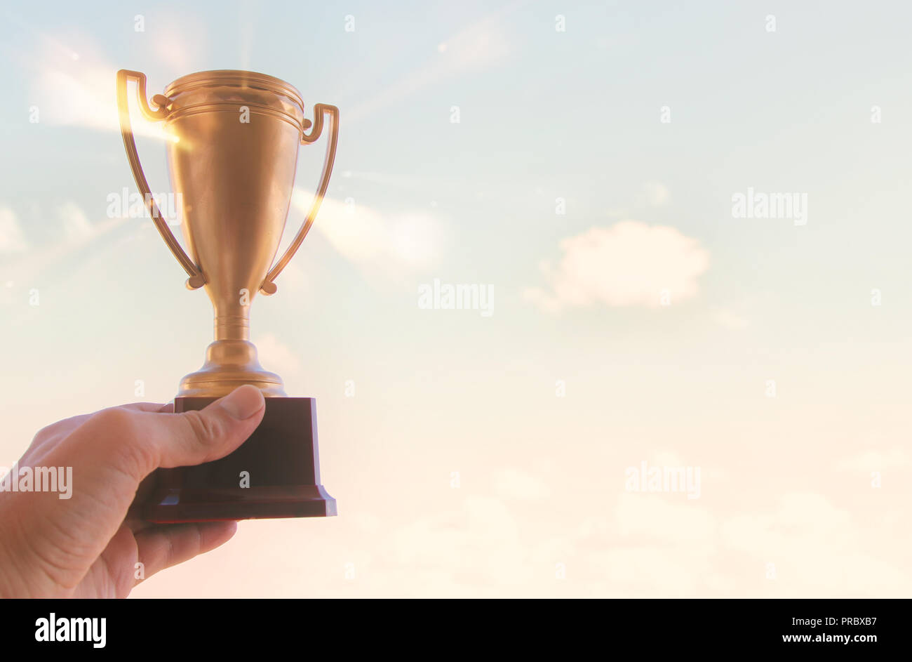 man hand raised, holding gold medal against sky. award and victory ...