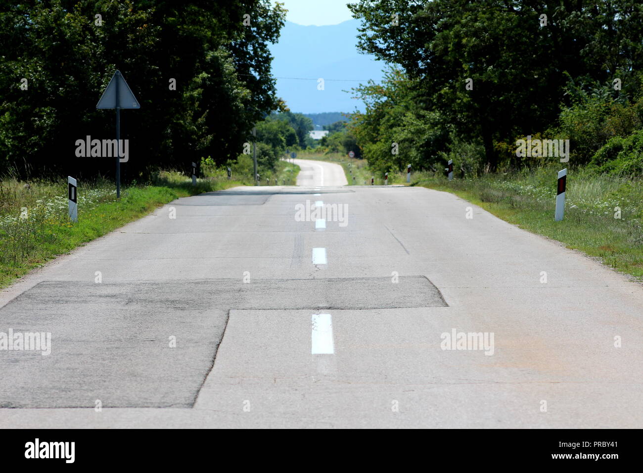 Asphalted country road with dotted white line in middle and patches ...