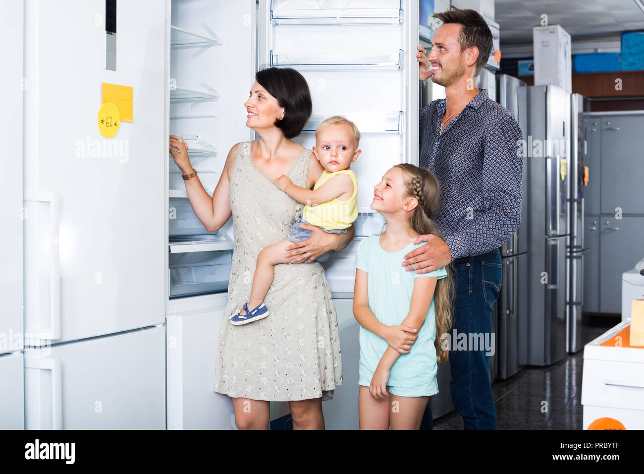 smiling family with two children choosing fridge in household store ...