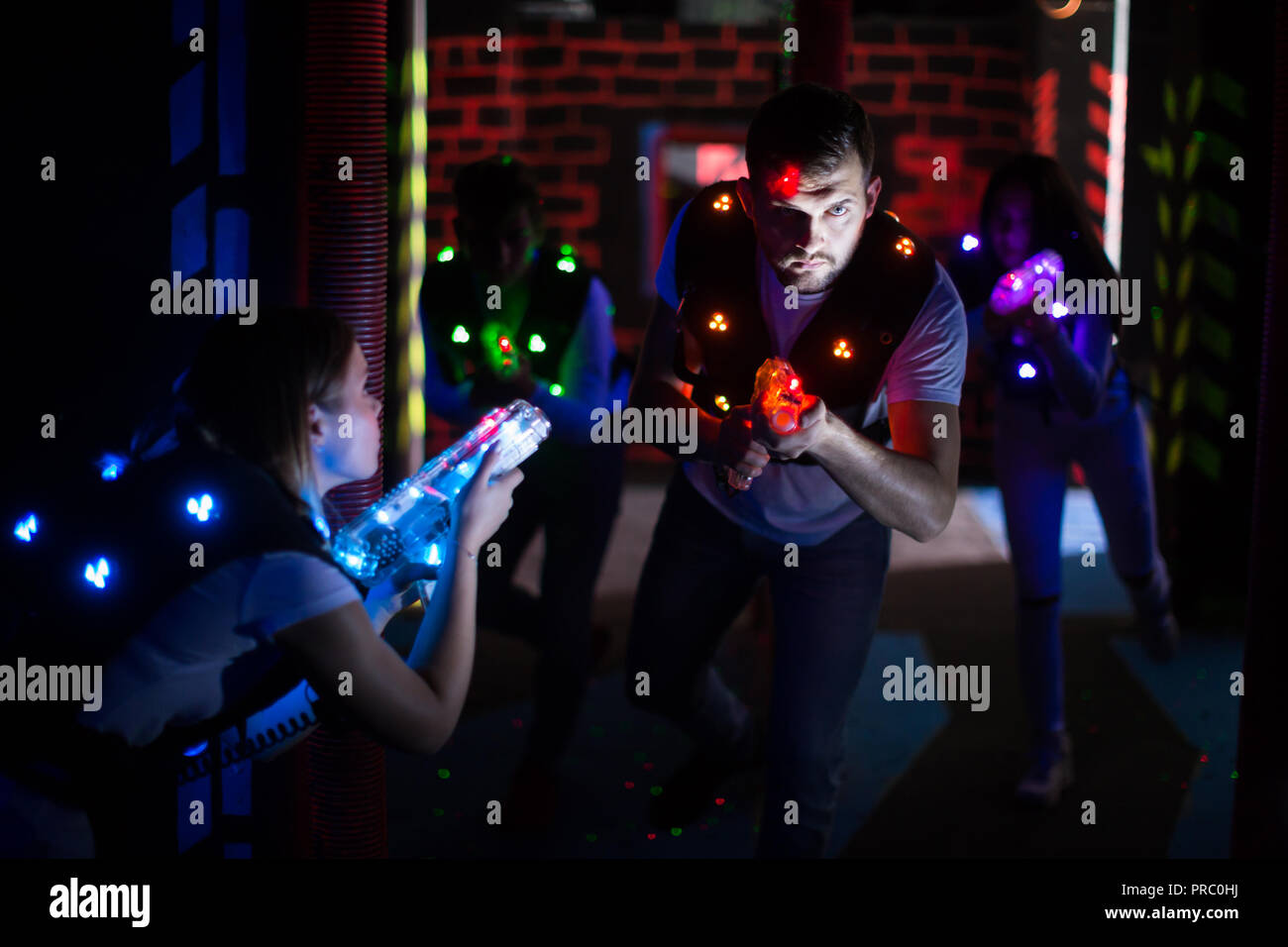 Emotional guy with laser pistol playing laser tag with friends on dark ...
