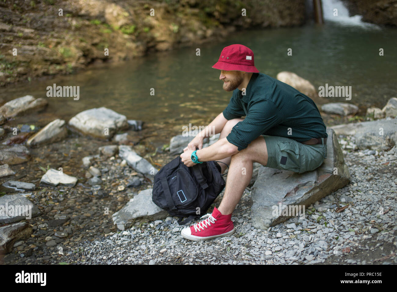 Tourist guy with backpack sitting near lake in a wild summer wood ...