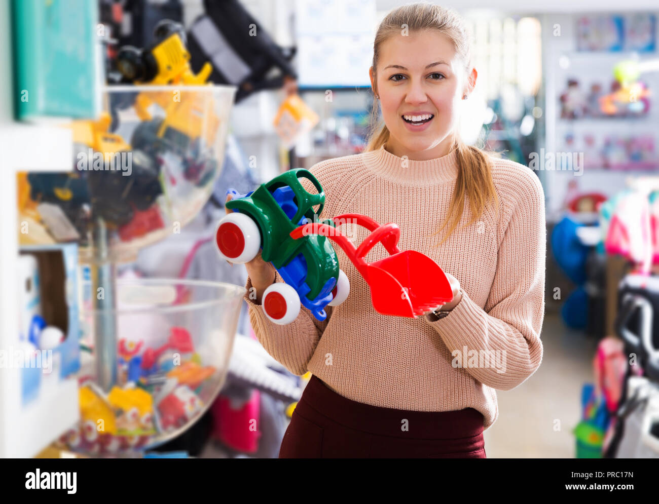 positive female consumer with children's plastic toys in the kids store ...