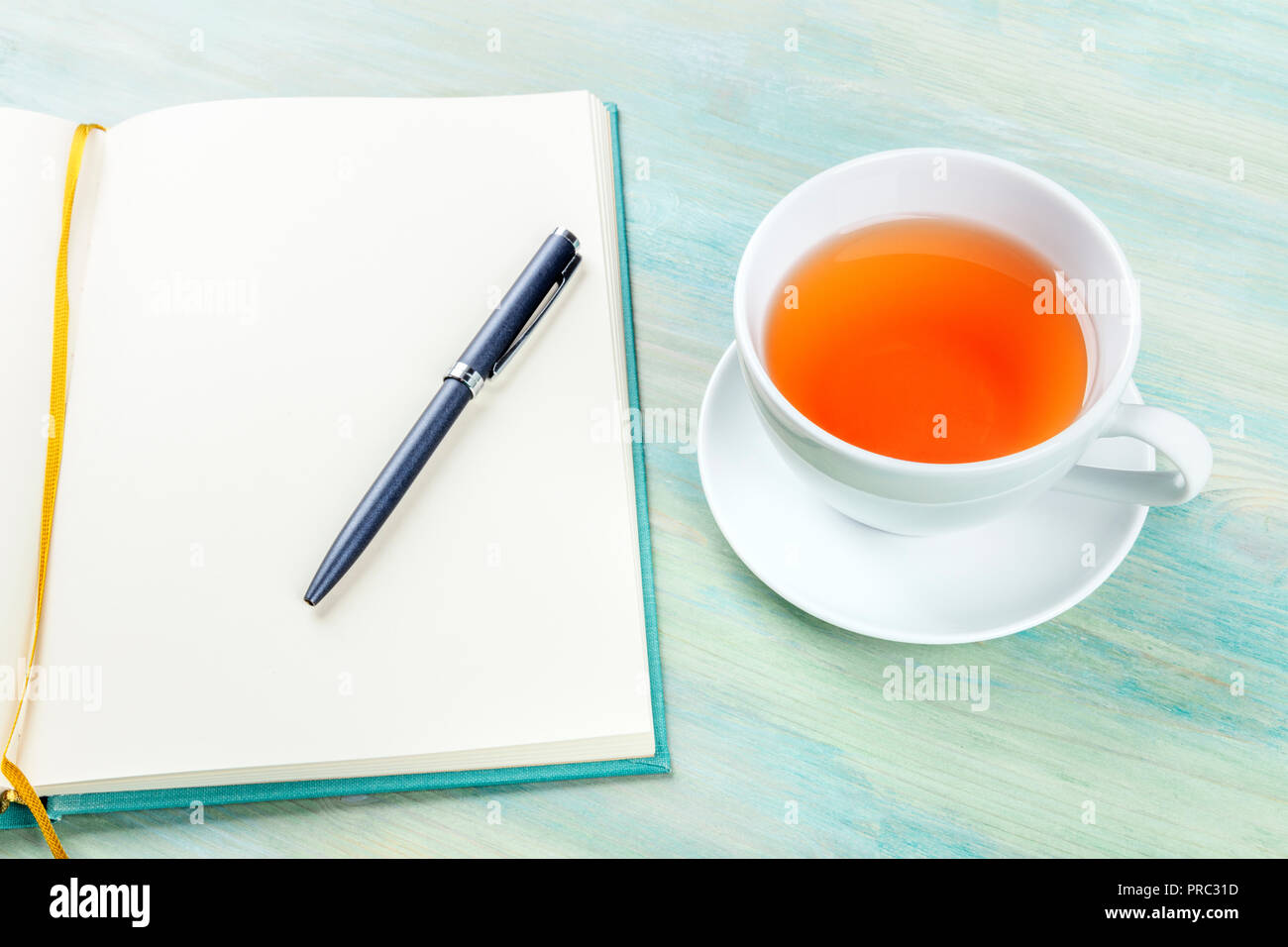 A photo of an open journal with a pen and a cup of tea, shot on a teal ...