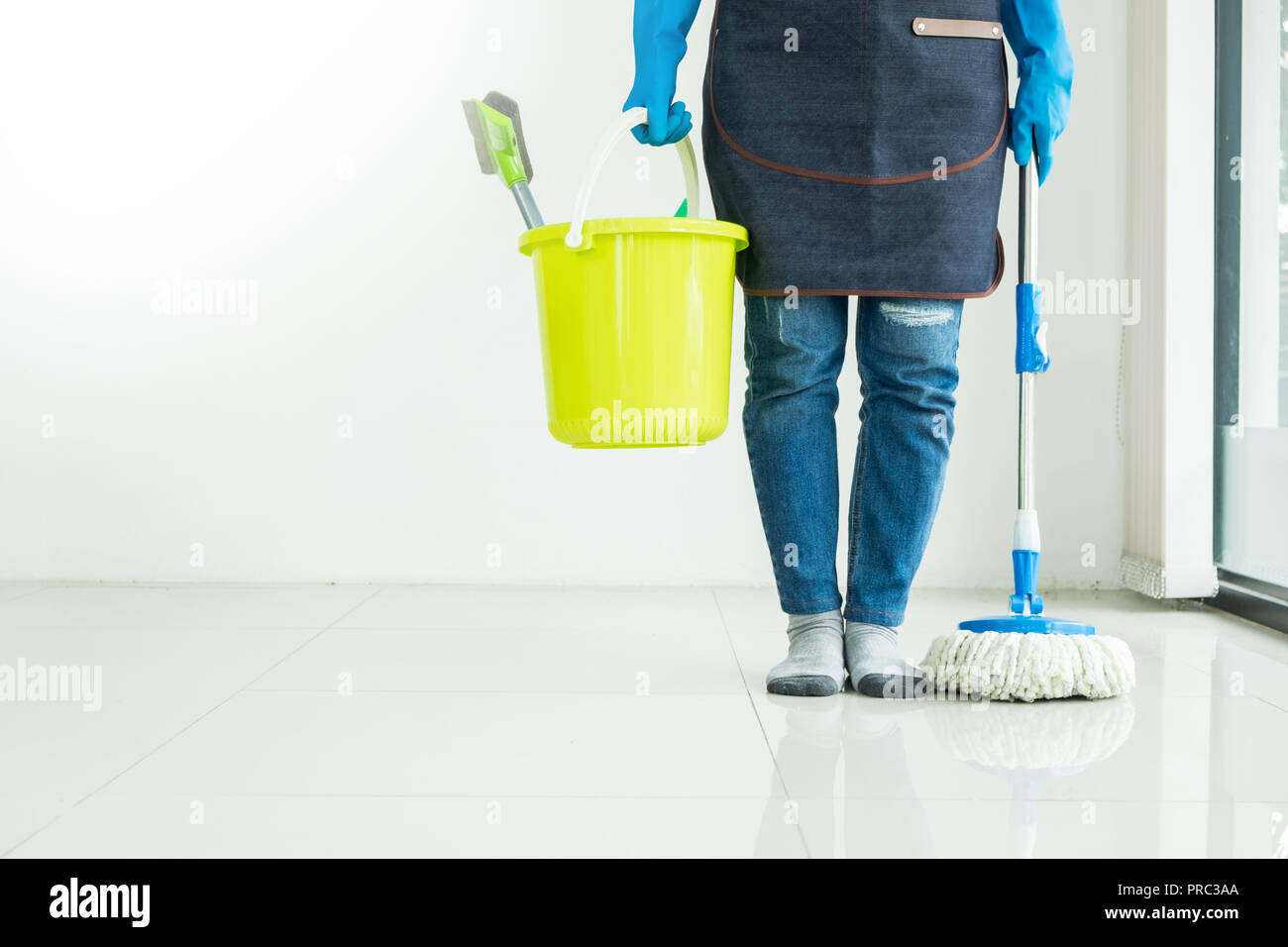 Young housekeeper cleaning floor mobbing holding mop and plastic bucket ...